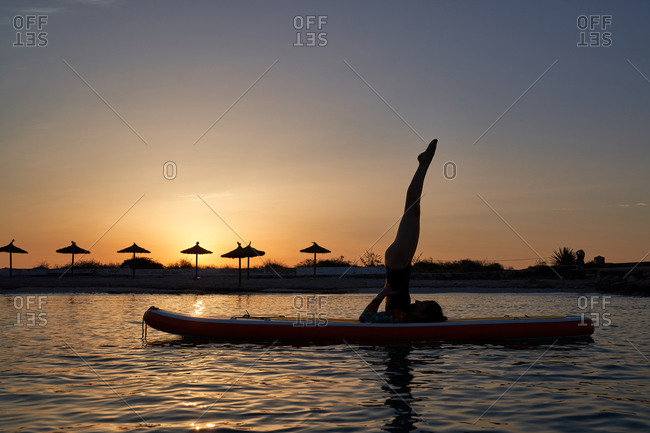 Side view of woman surfer practicing yoga on surfboard in sea during ...