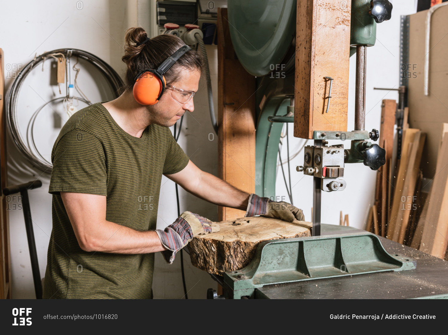 Focused male carpenter in protective ear muffs and goggles cutting ...