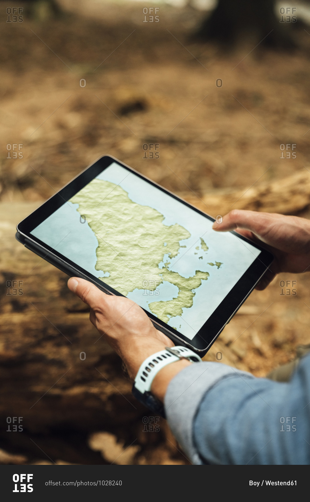Close-up of man's hands analyzing map over digital tablet in forest ...