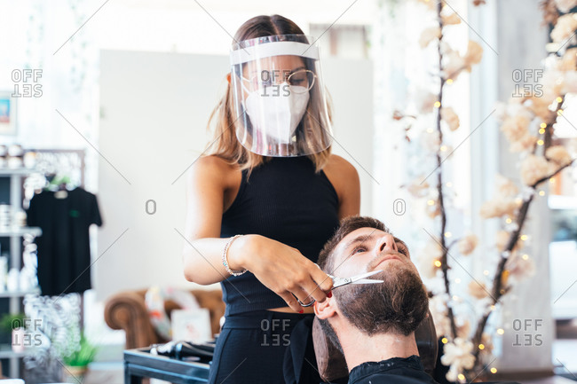 Professional female barber in protective mask and face shield cutting ...