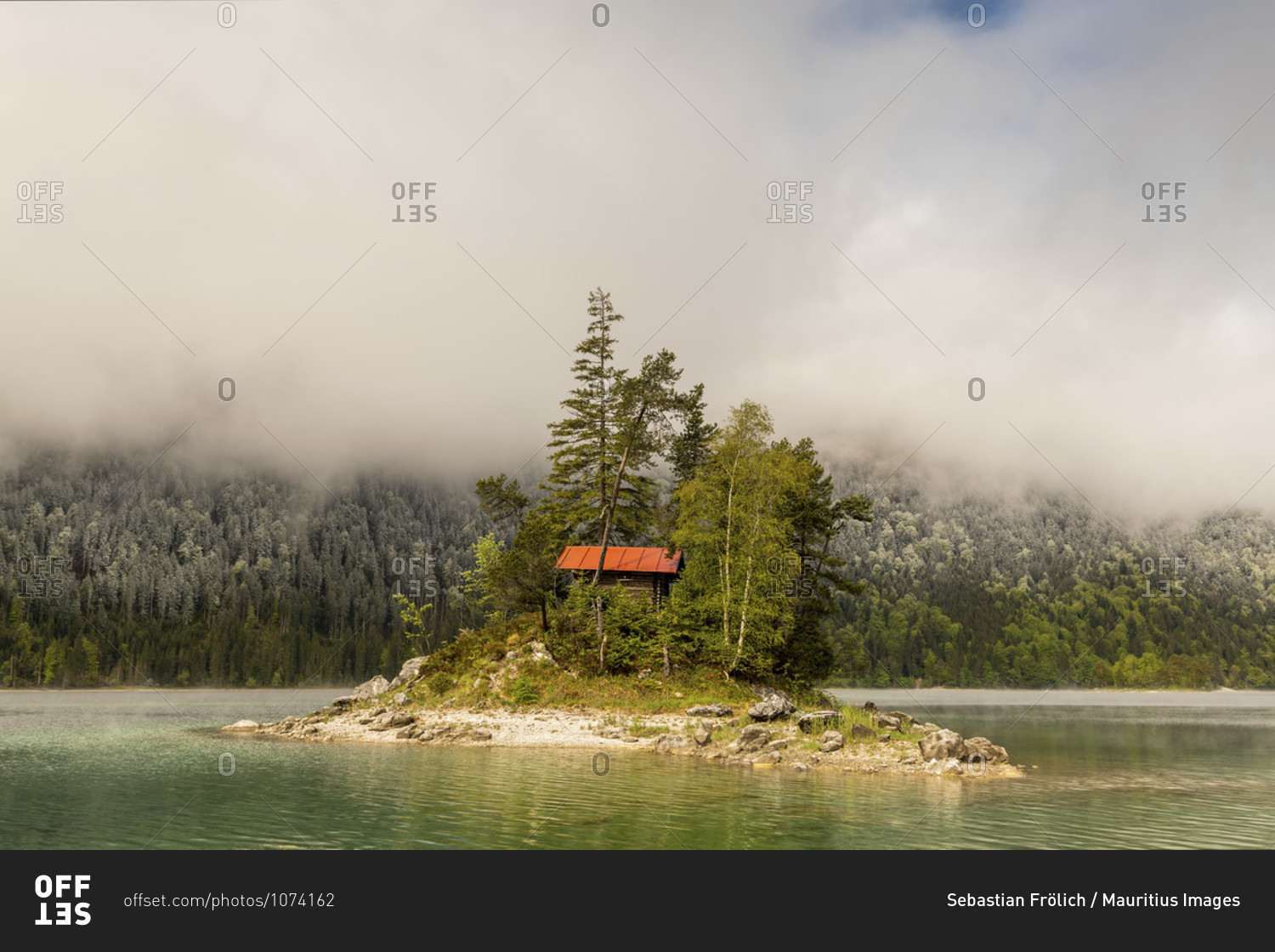 A small lonely island with a log cabin and red roof, in the middle of ...