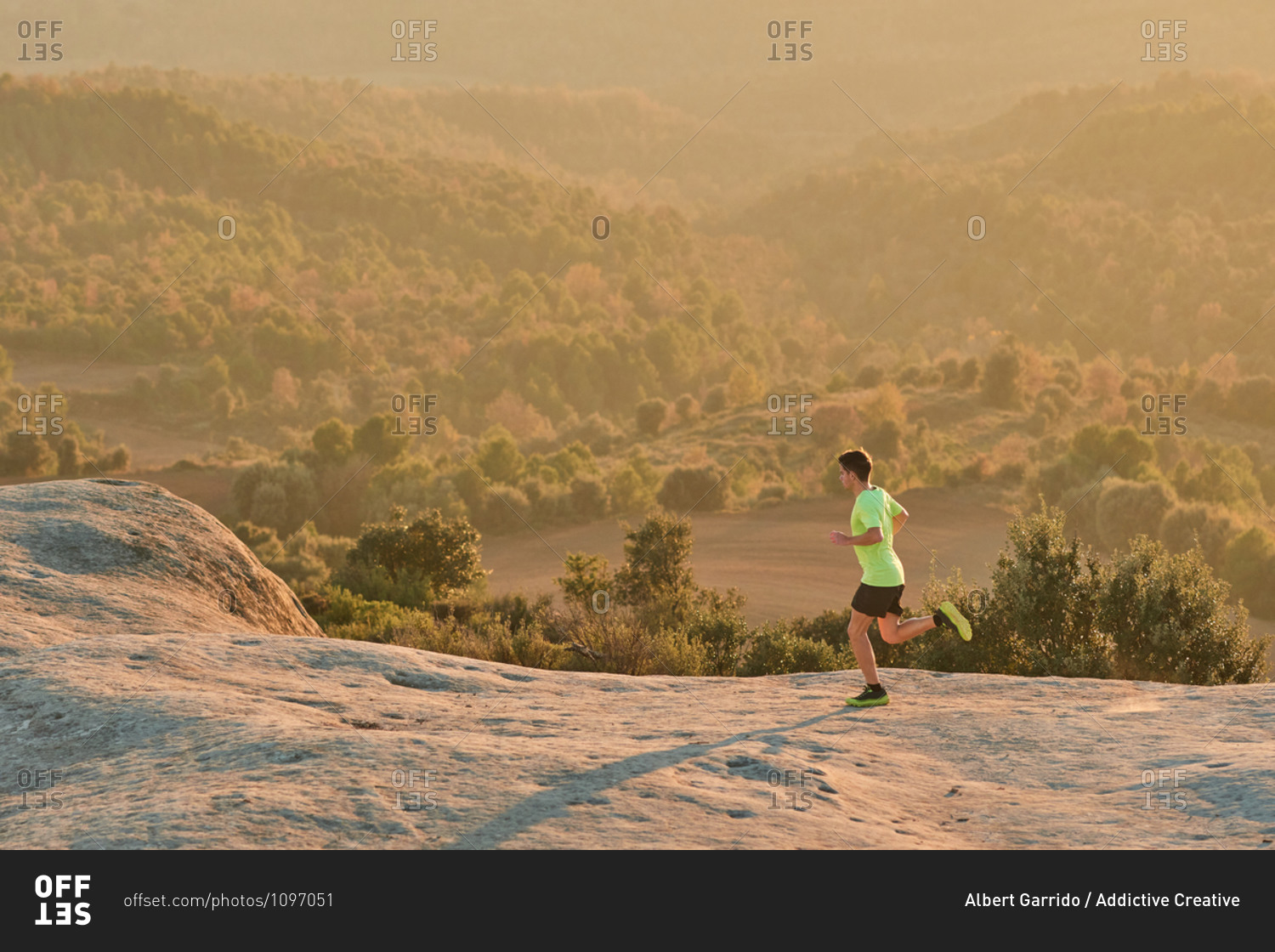 Side view of slim male runner running on rocks in mountains at sunset ...