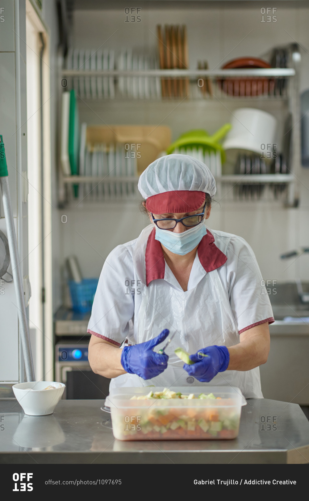 Female cook in white uniform and protective mask and gloves cutting ...