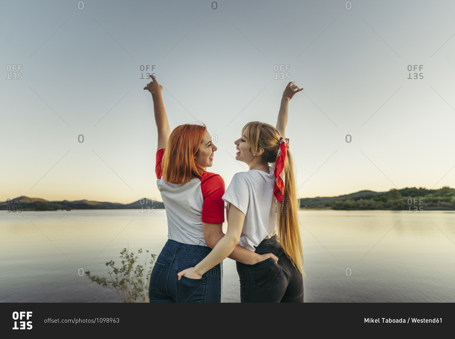 Smiling Lesbian Couple Standing With Hands In Pockets Against Clear Sky