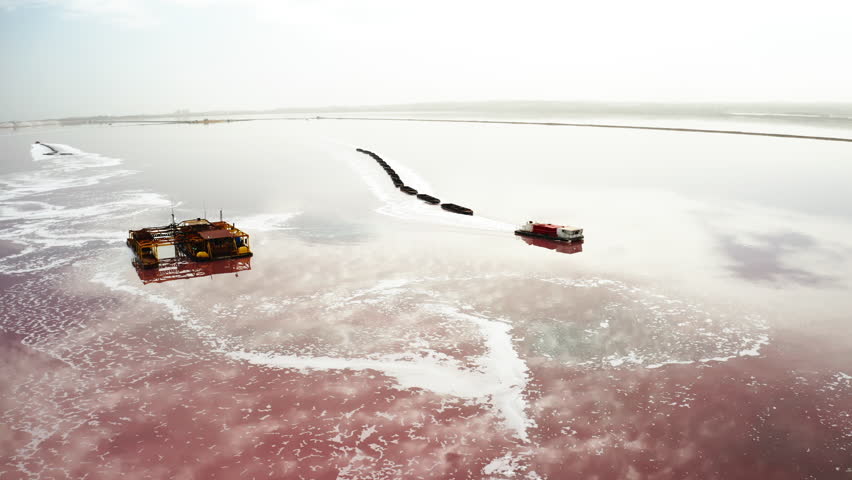 Barge pulls cargo past salt mining platform on pink Torrevieja lake ...
