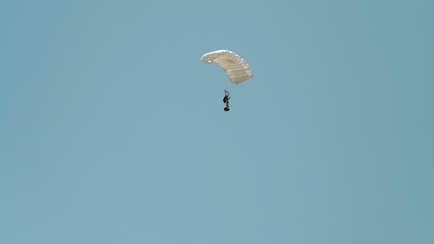 A military paratrooper in full gear is descending through the sky under ...